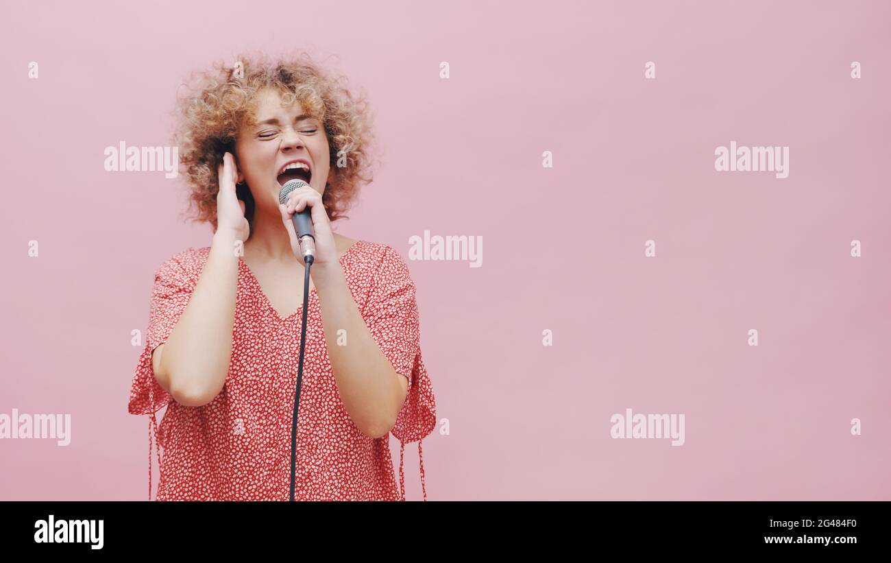 Cute girl singing loudly with a microphone in her hand. Hand on her ear ...