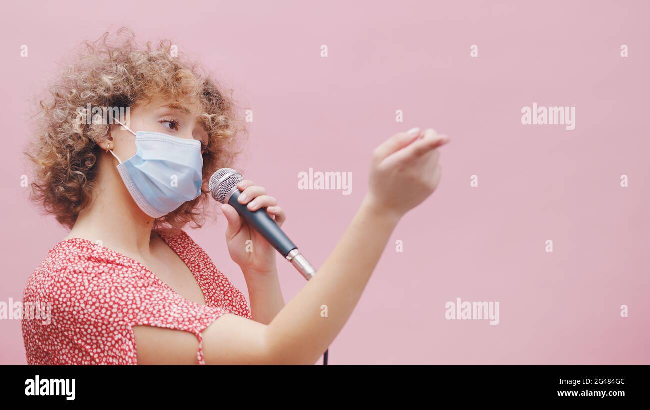 Cute girl singing with a microphone in her hand. Wearing a face mask ...