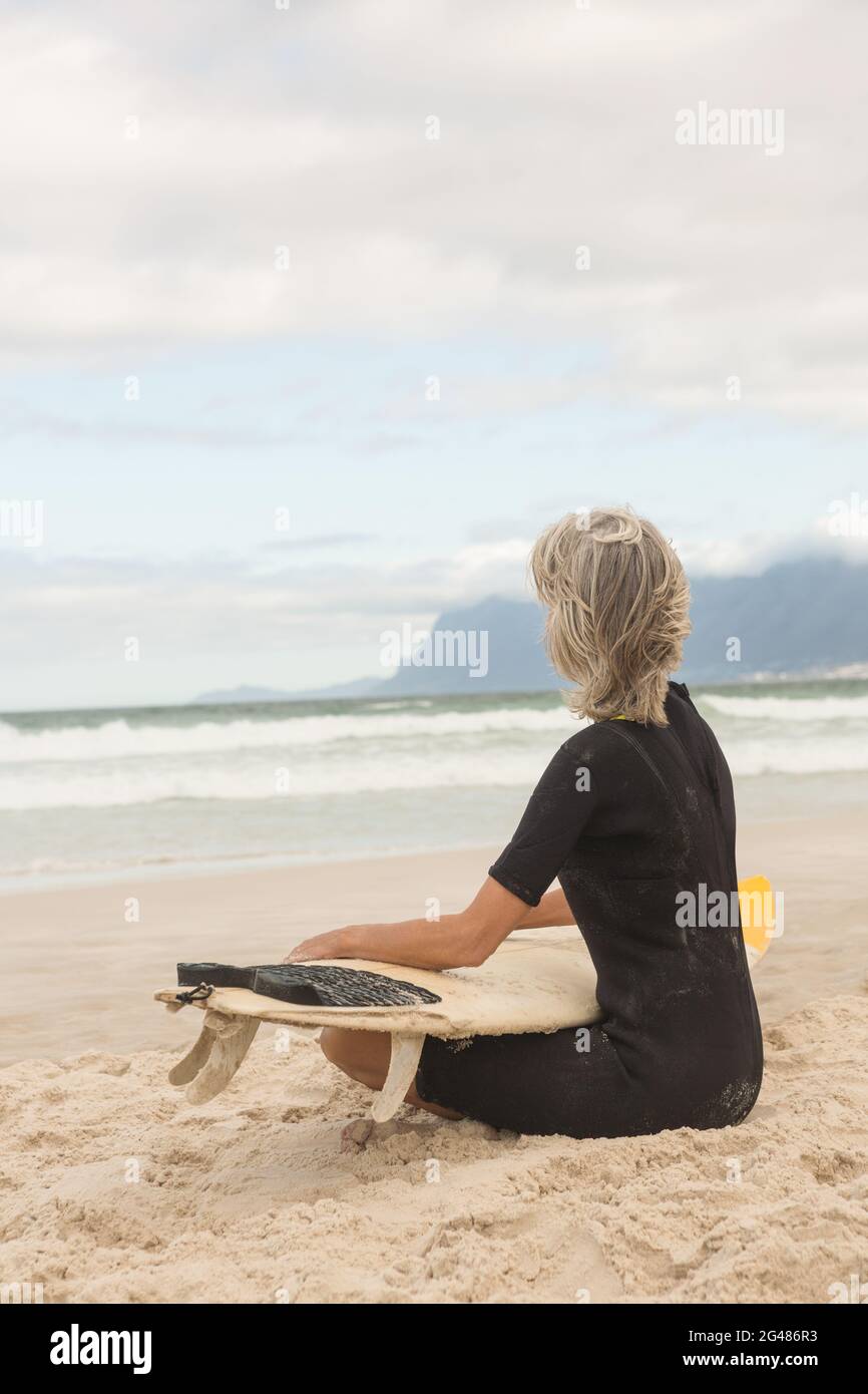 Side view of woman in wetsuit sitting with surfboard Stock Photo - Alamy
