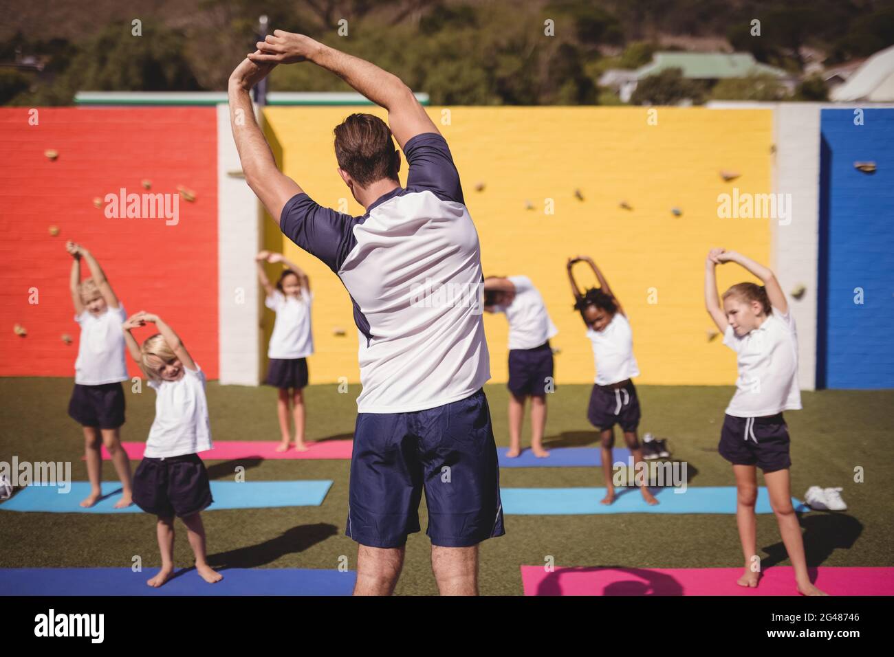Coach teaching exercise to school kids Stock Photo - Alamy
