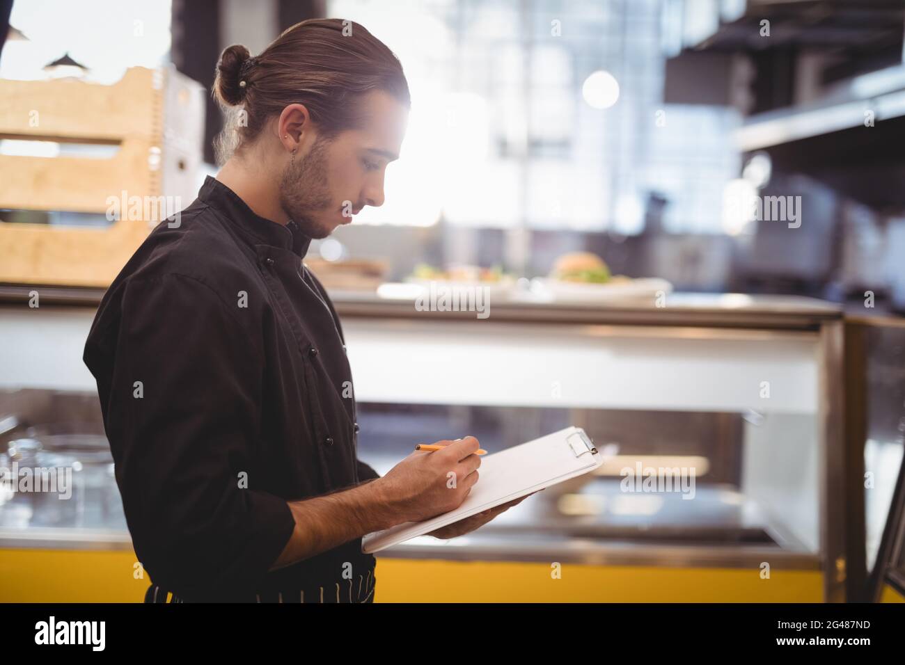 Side view of young waiter writing on clipboard Stock Photo - Alamy