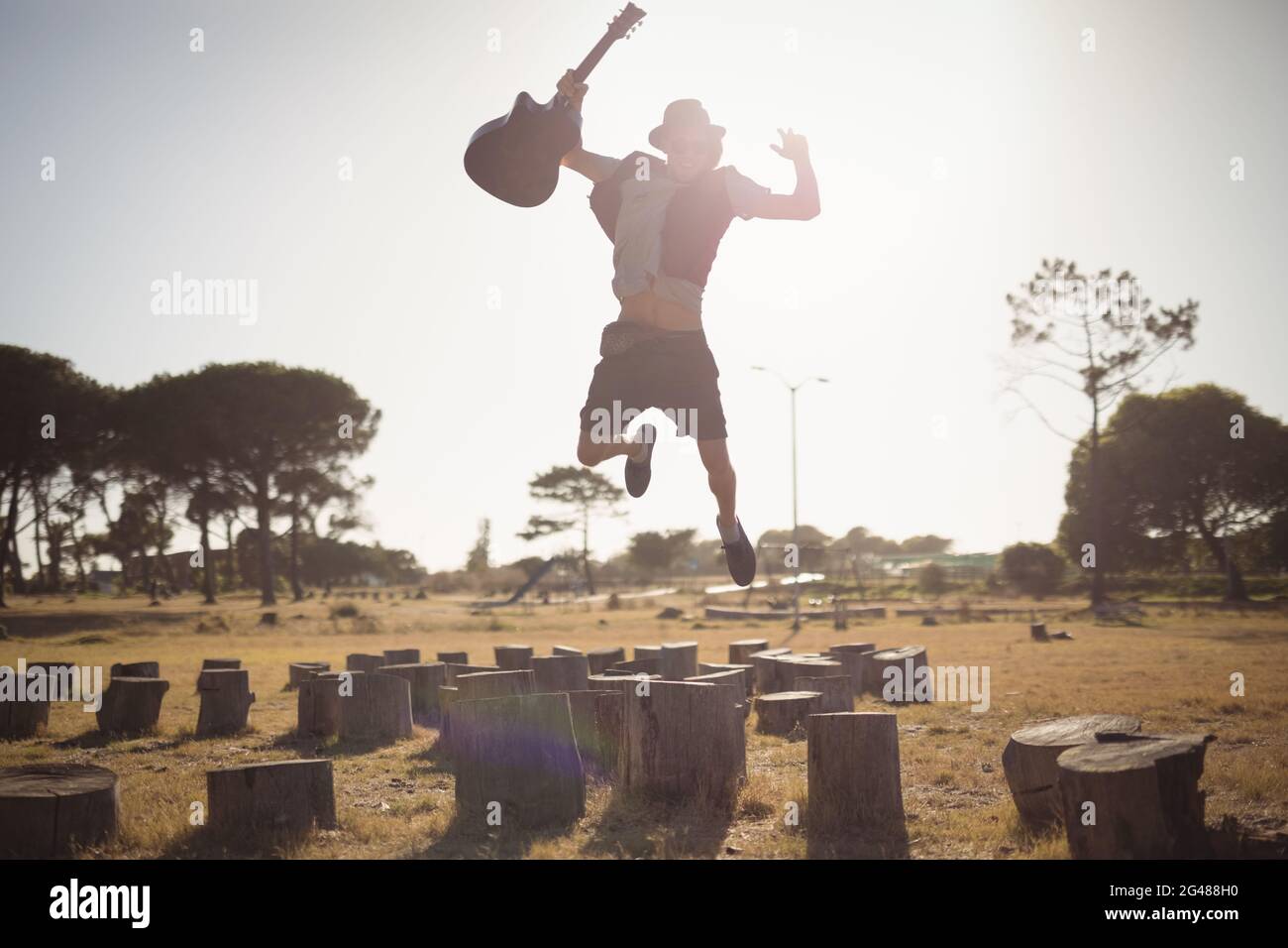 Young man holding guitar while jumping on tree stump Stock Photo - Alamy