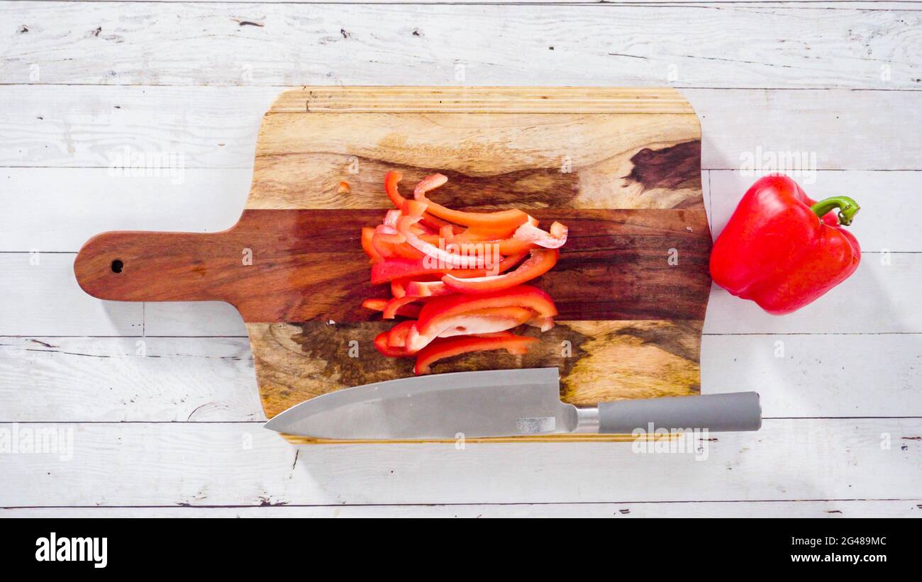 Flat lay. Mincing organic red bell peppers on a wood cutting board ...