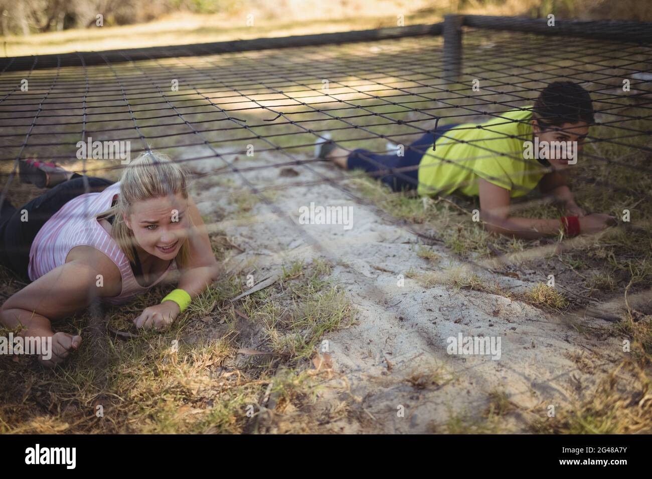 Determined women crawling under the net during obstacle course Stock ...
