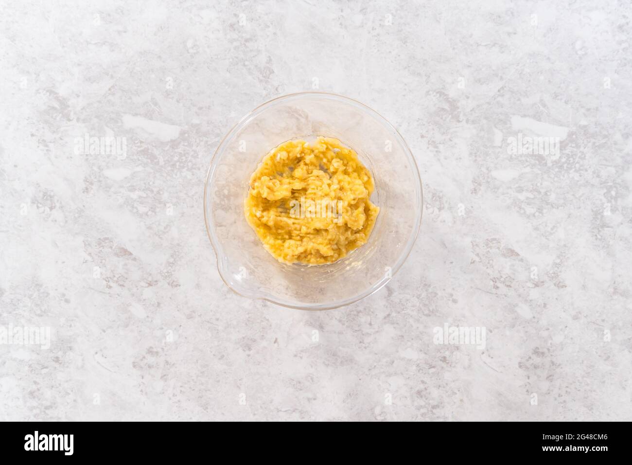 Smashing riped bananas in a glass mixing bowl to prepare coconut banana ...