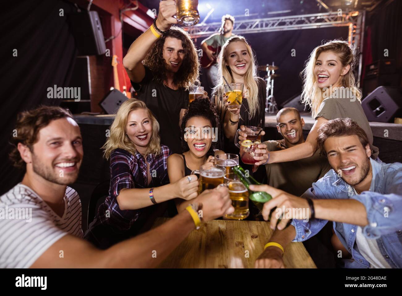 Portrait of cheerful friends toasting drink at table with performer ...