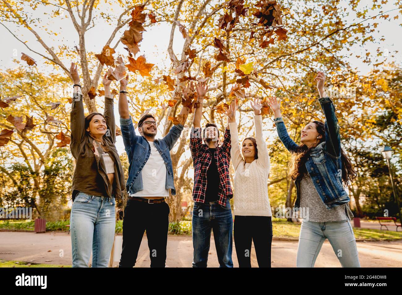 Group of friends in the park having fun throwing leaves in the air ...