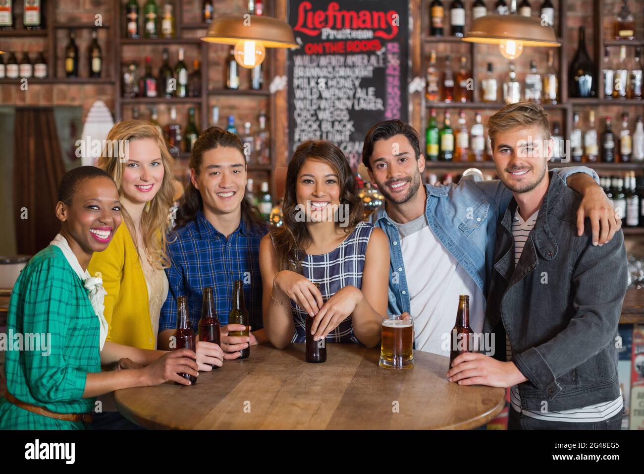 Portrait of young friends with beers by table in pub Stock Photo - Alamy