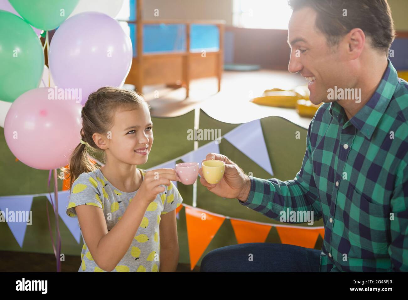 Father and girl toasting their tea cups while playing with toy kitchen ...