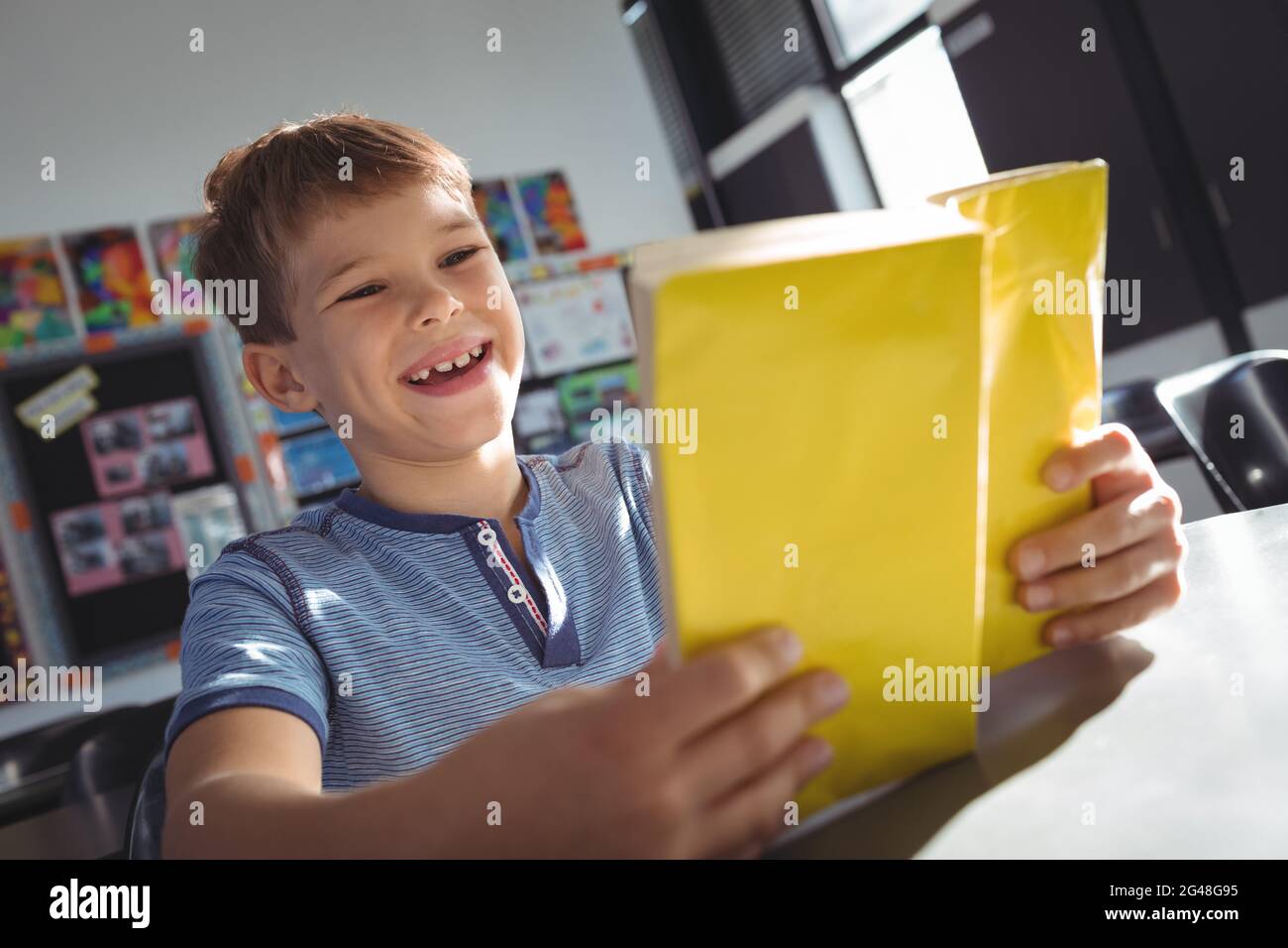 Happy boy reading book in classroom Stock Photo - Alamy