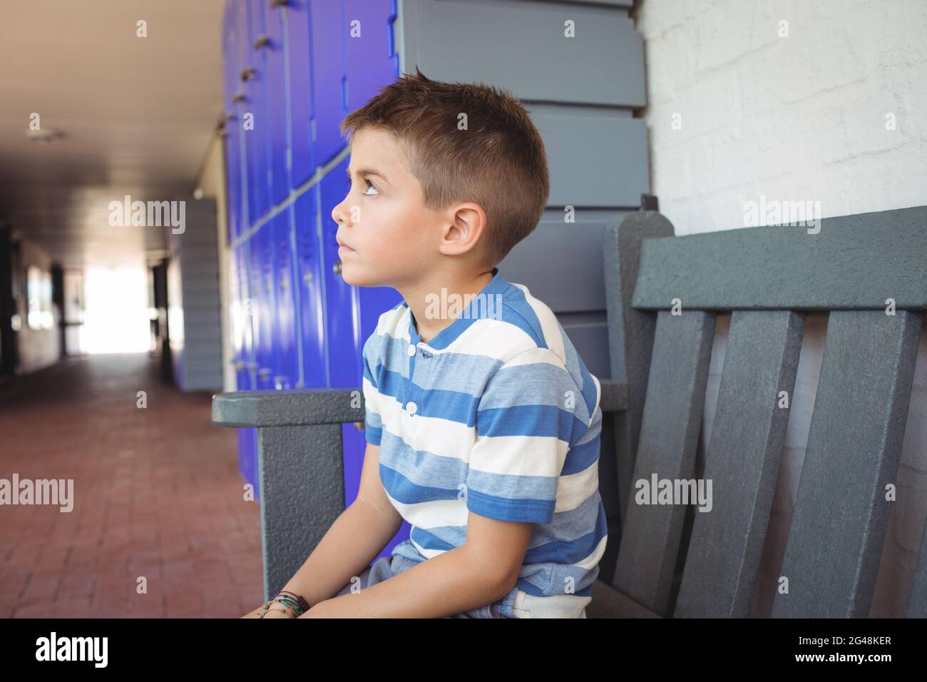 Thoughtful boy sitting on bench in corridor Stock Photo - Alamy