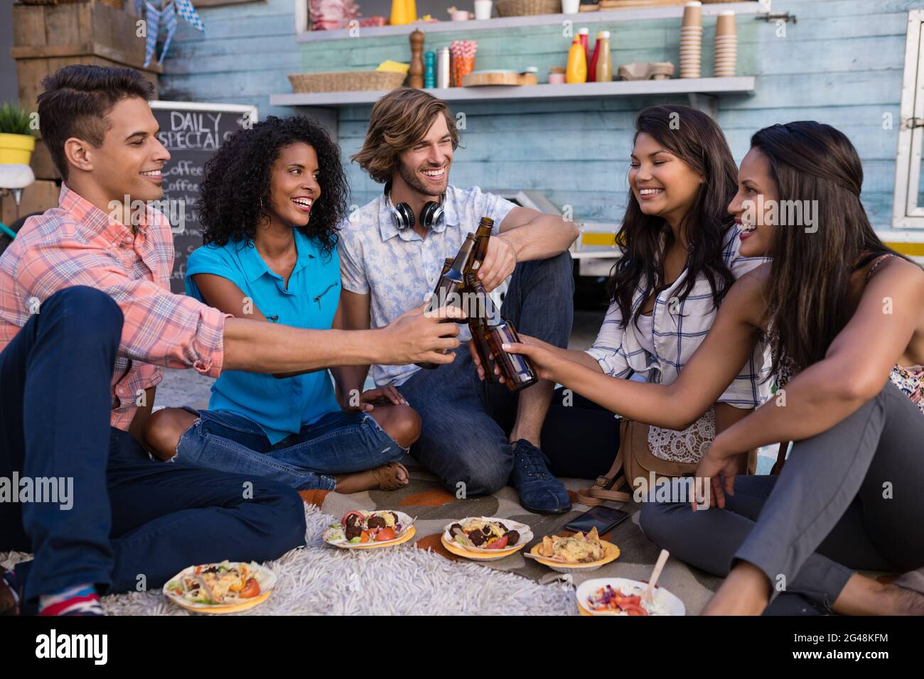 Group of friends toasting beer bottles while having meal Stock Photo ...