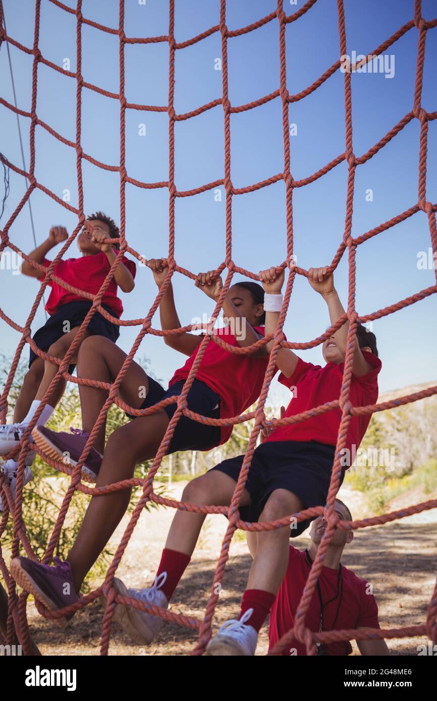 Trainer assisting boy to climb a net during obstacle course training ...