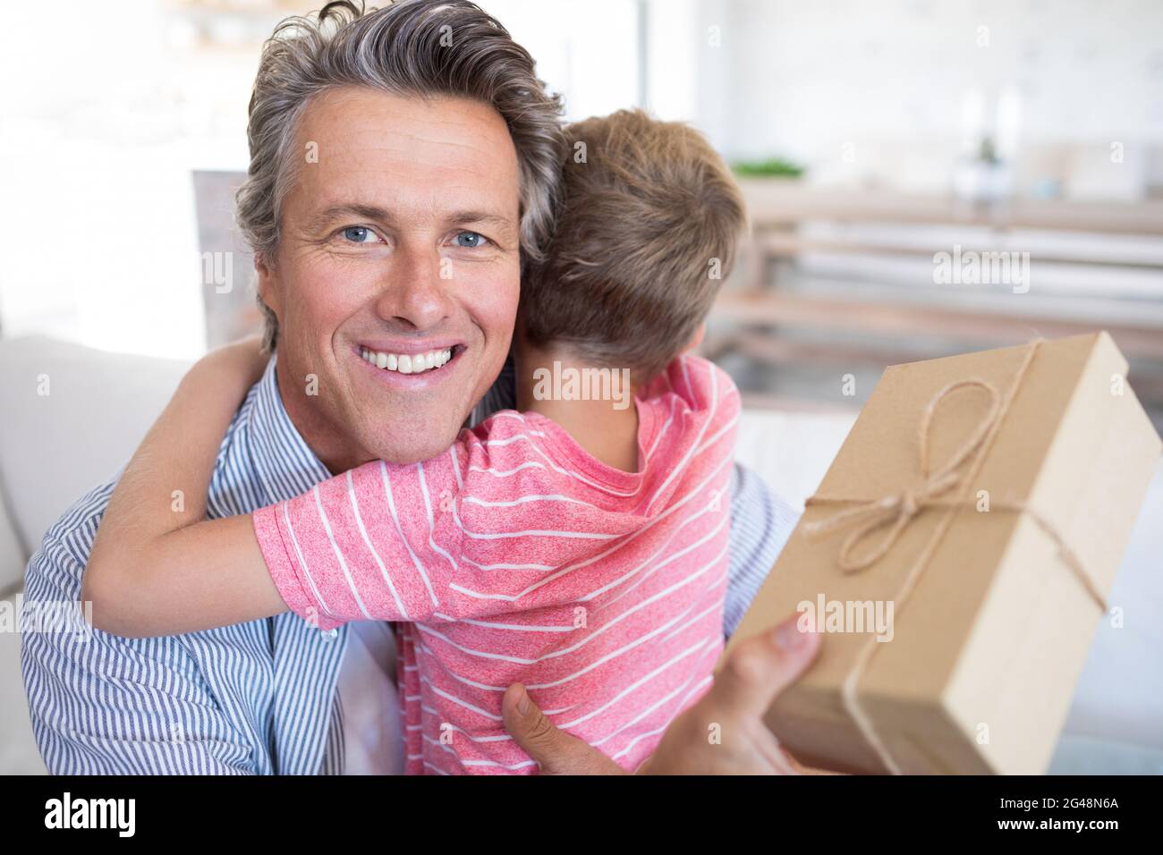 Father embracing son while receiving gift in living room Stock Photo ...