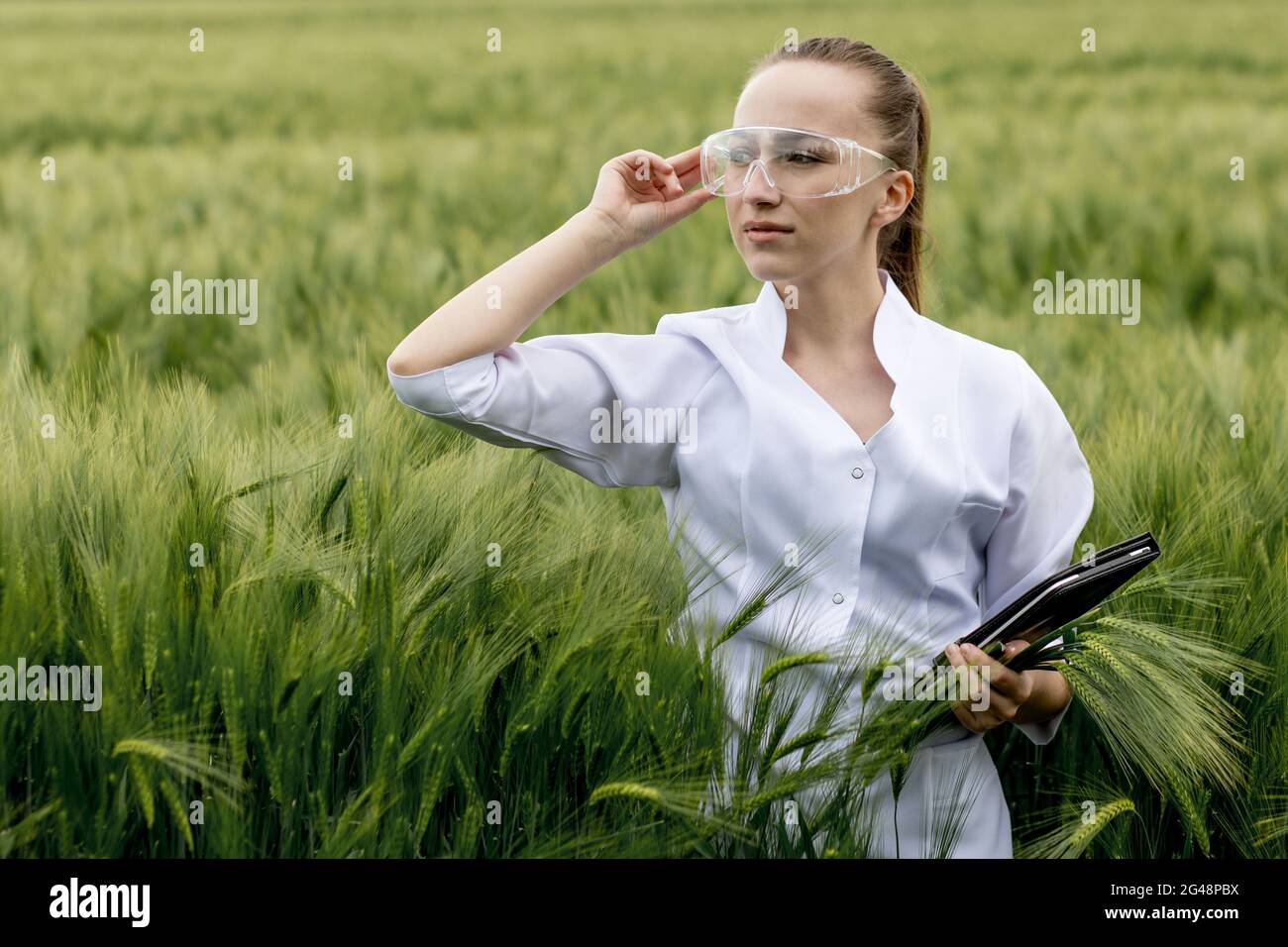 Young female ecologist scientist in goggles standing in green field and ...
