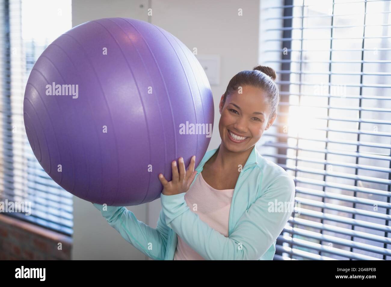 Portrait of smiling young female doctor holding purple exercise ball ...