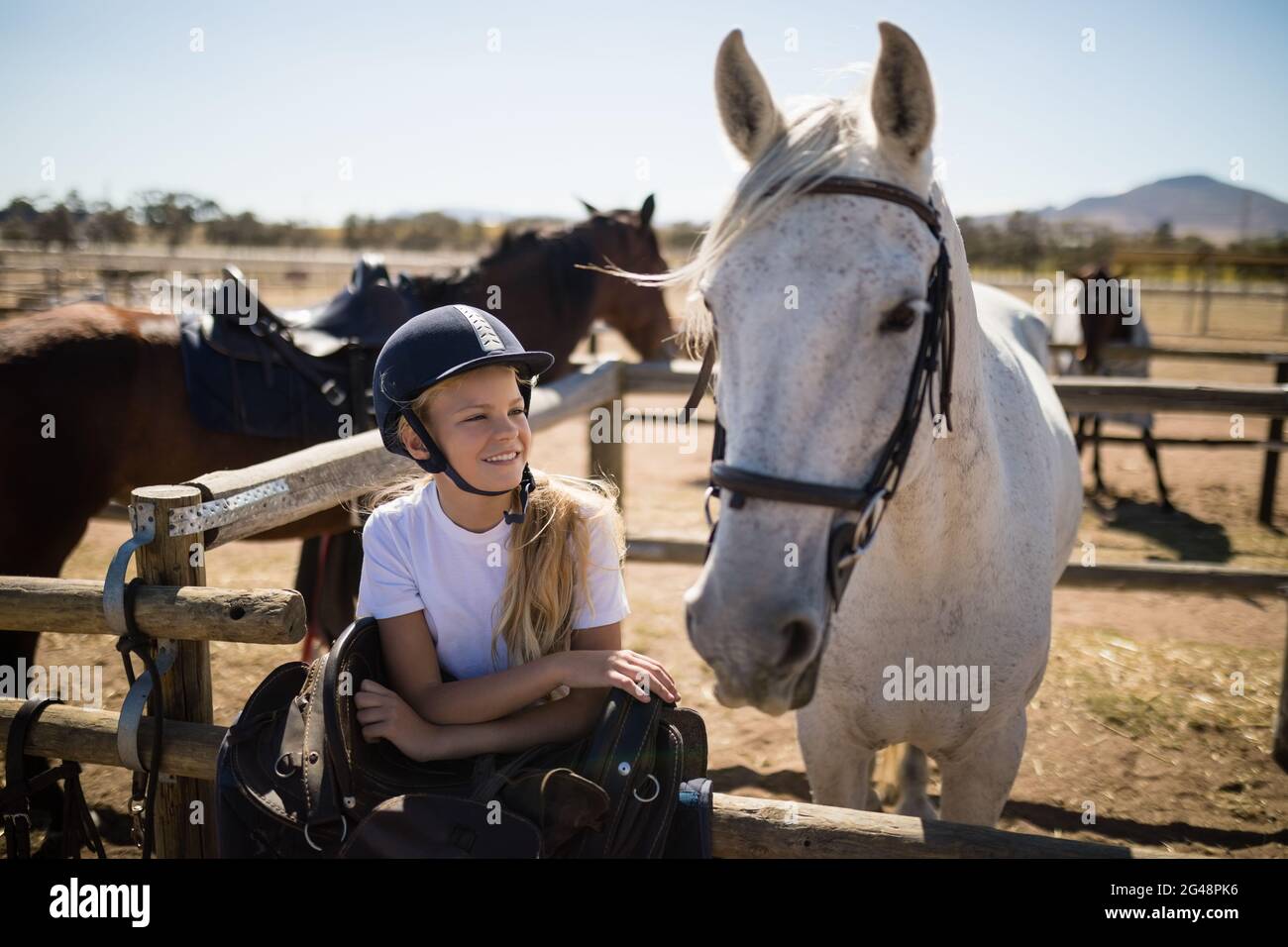 Smiling girl leaning on the fence and looking at the white horse in ...