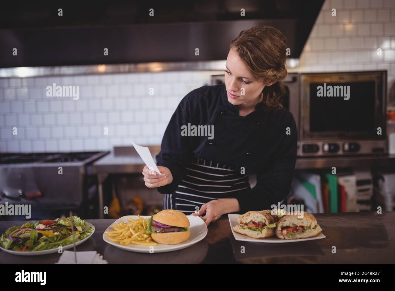 Confident young waiter holding paper while standing with fresh meal at ...
