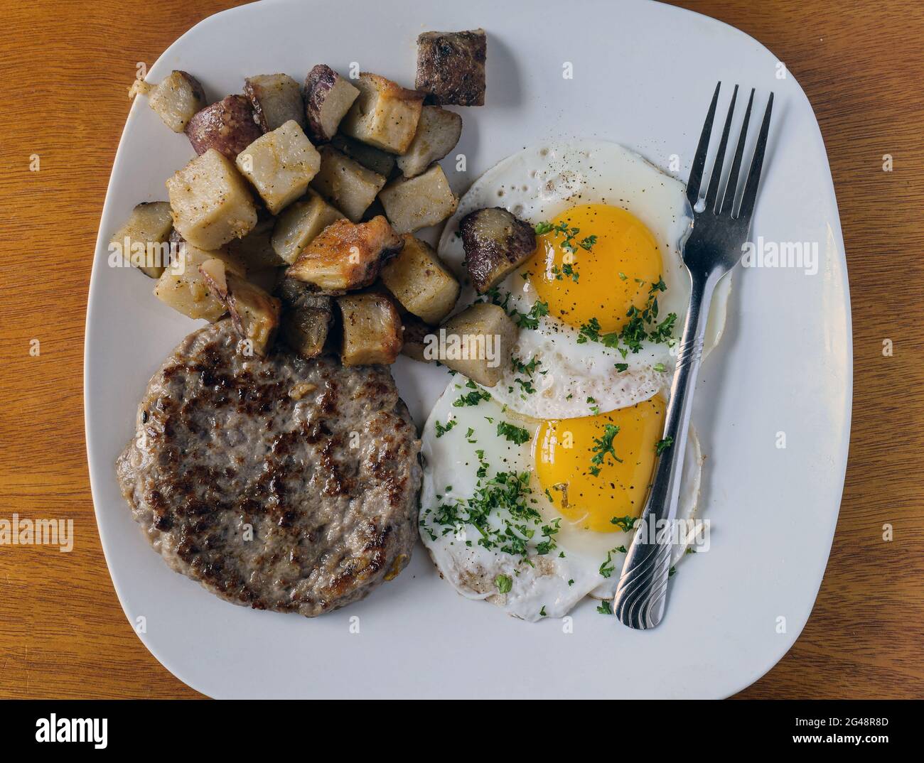 fried eggs top with parsley and served with sausage patty and home ...