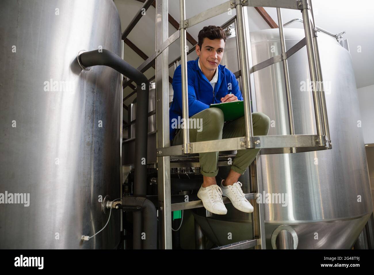 Full length portrait of worker amidst storage tanks writing on ...