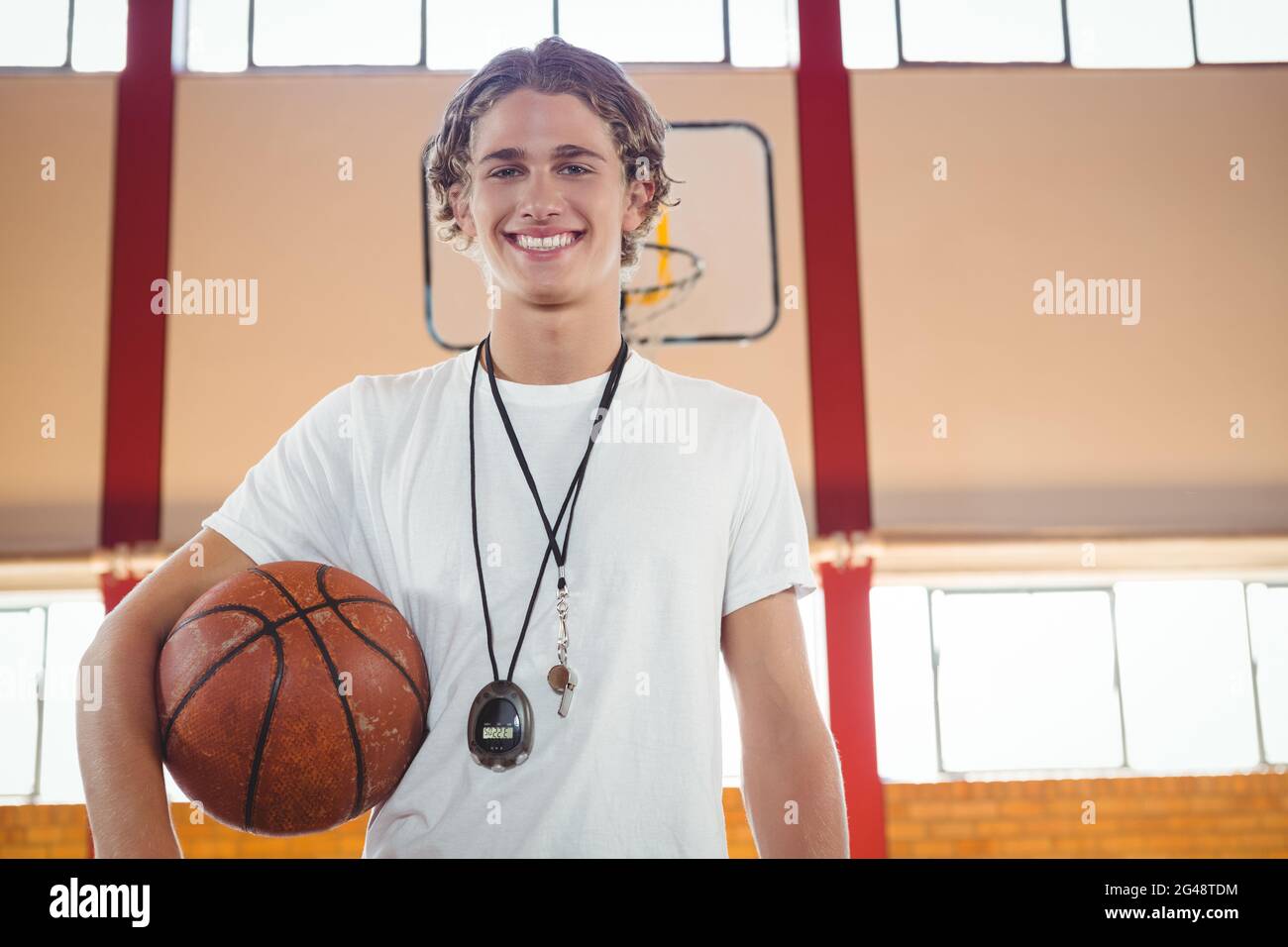 Portrait of happy male coach standing against basketball hoop Stock ...