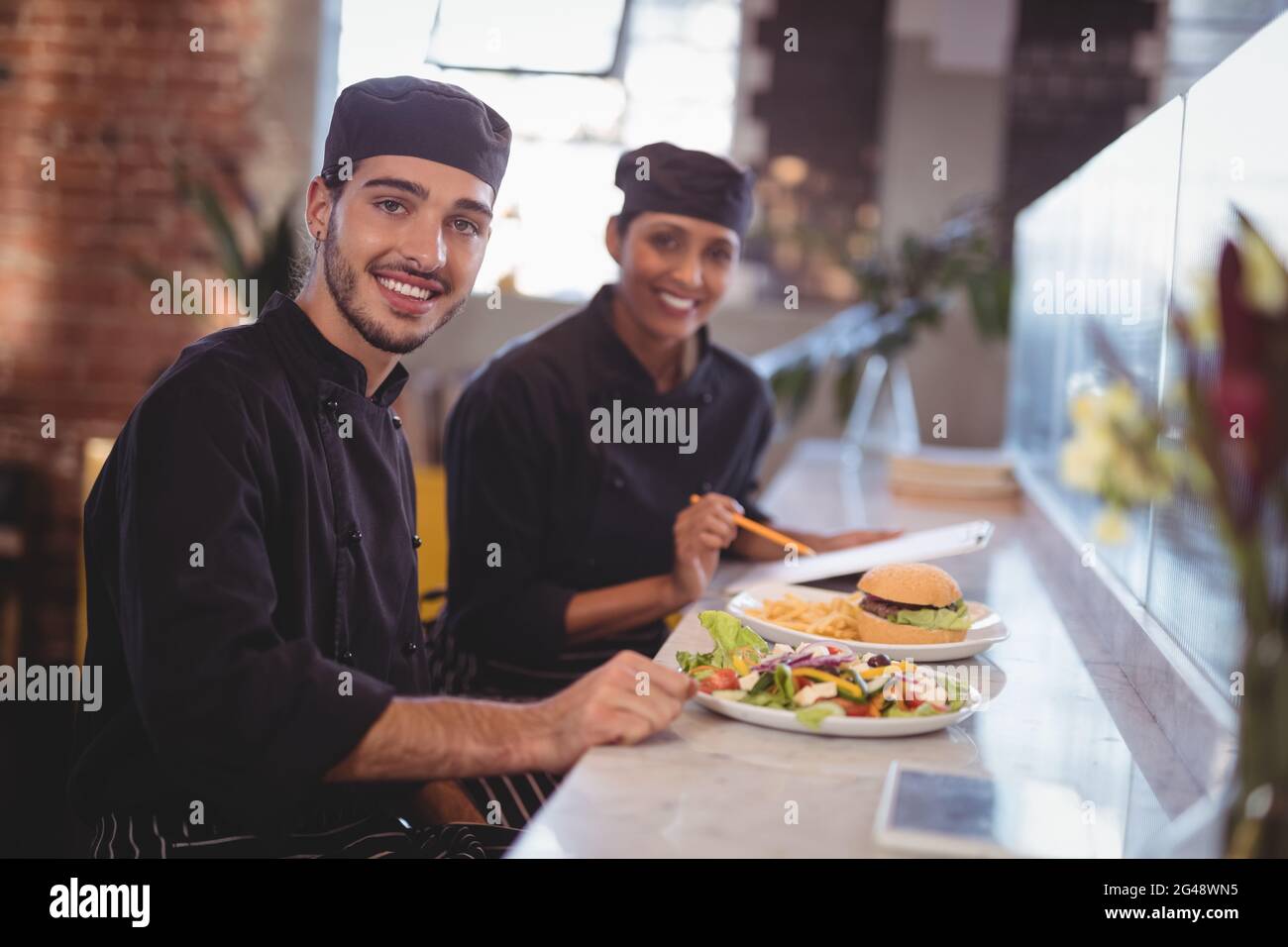 Portrait of smiling young wait staff sitting with food and clipboard at ...