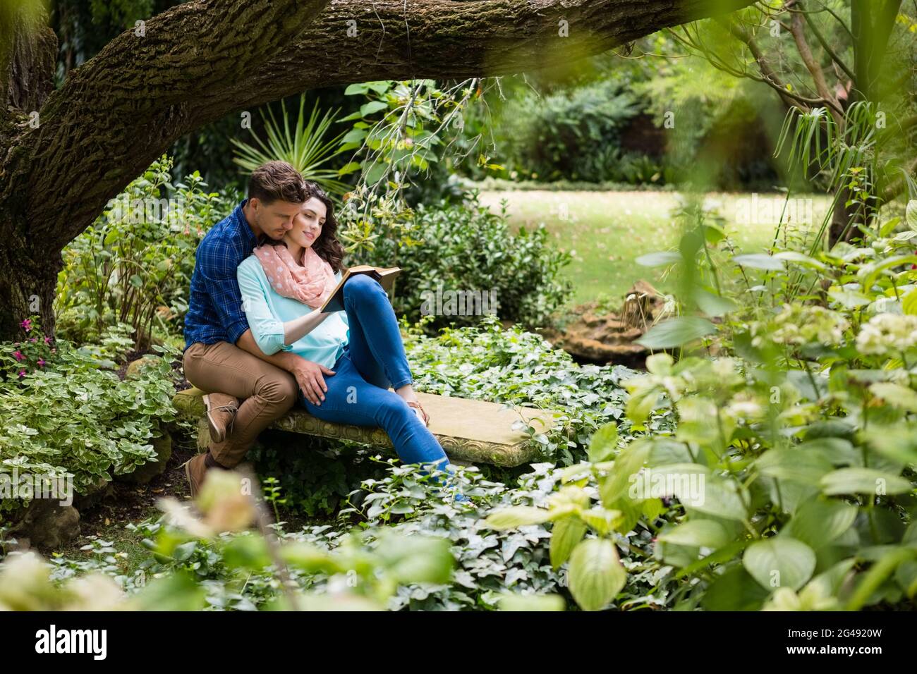 Romantic couple reading book on bench in garden Stock Photo - Alamy
