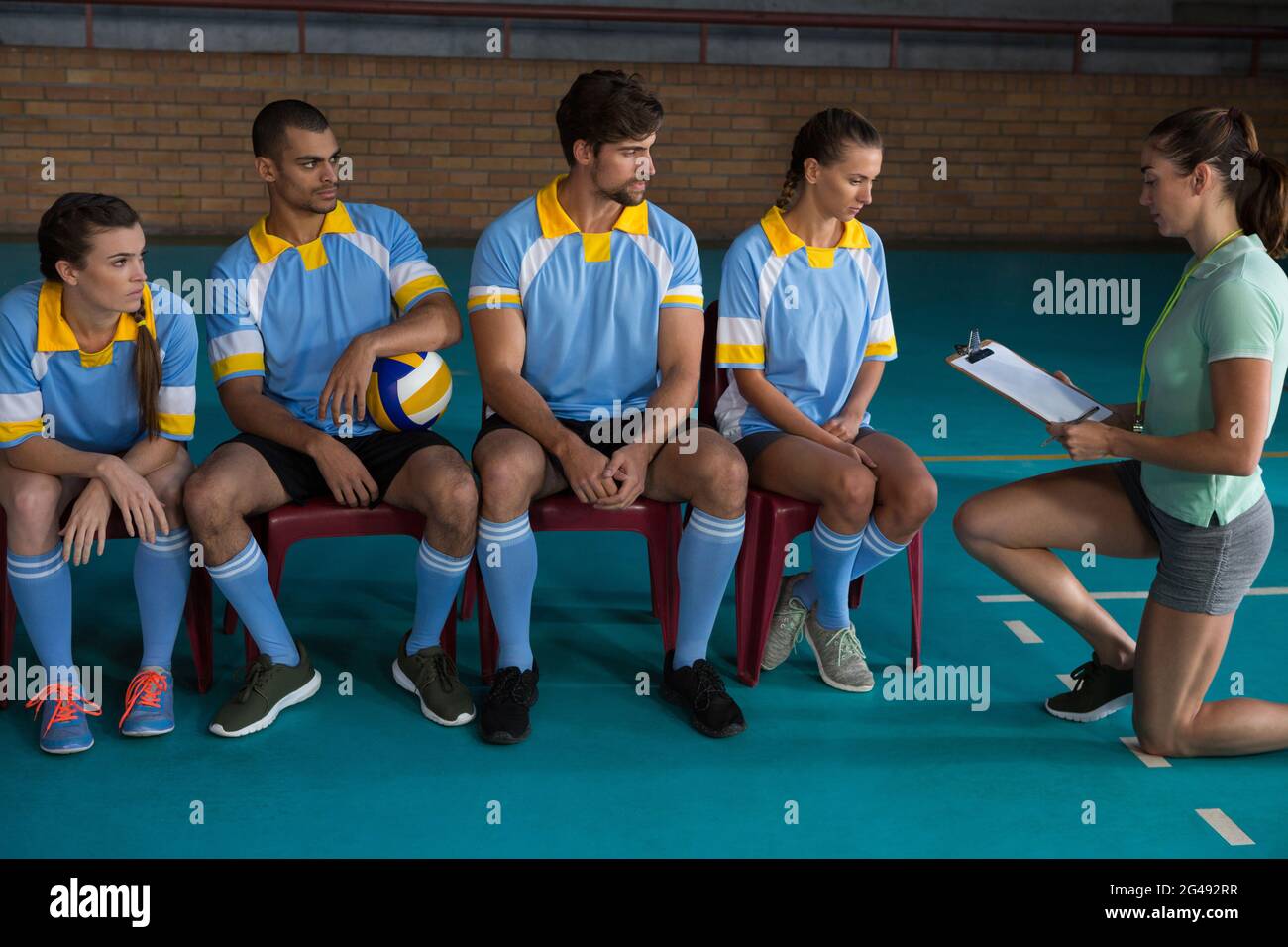 Coach discussing with volleyball players sitting on chairs Stock Photo ...
