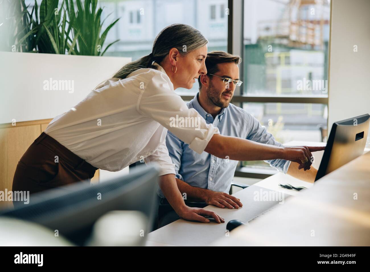 Mature woman working with young man sitting at desk and showing ...