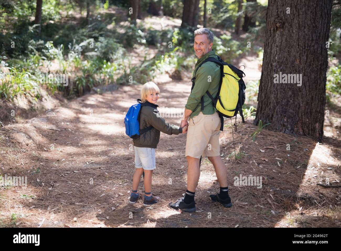 Smiling father and son carrying backpack while hiking in forest Stock ...