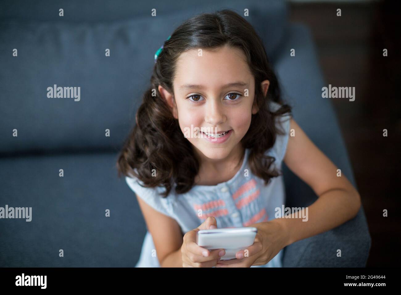 Happy girl sitting on sofa and using mobile phone in living room Stock ...