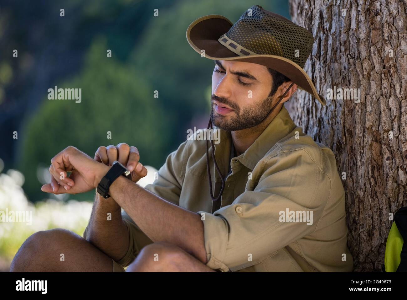 Man looking at his wrist watch while resting near the tree Stock Photo ...