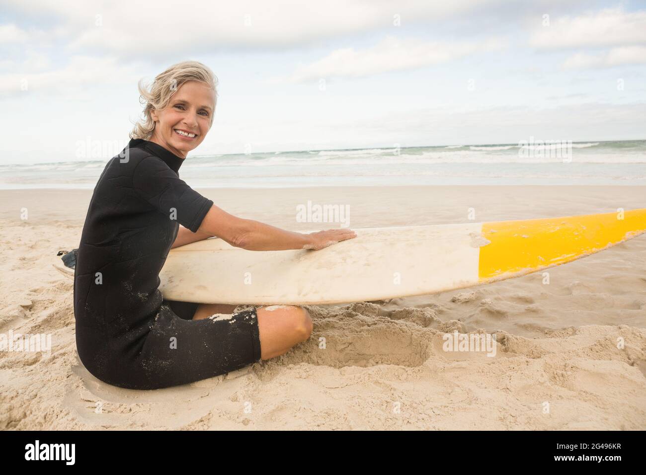 Portrait of smiling woman sitting with surfboard against sky Stock ...