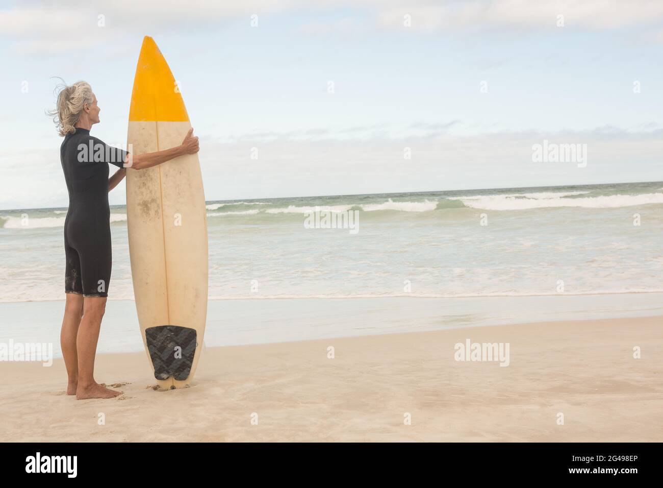 Rear view of senior woman holding surfboard while standing on shore ...