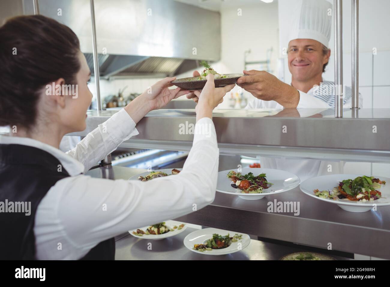 Chef handing food dish to waitress at order station Stock Photo - Alamy
