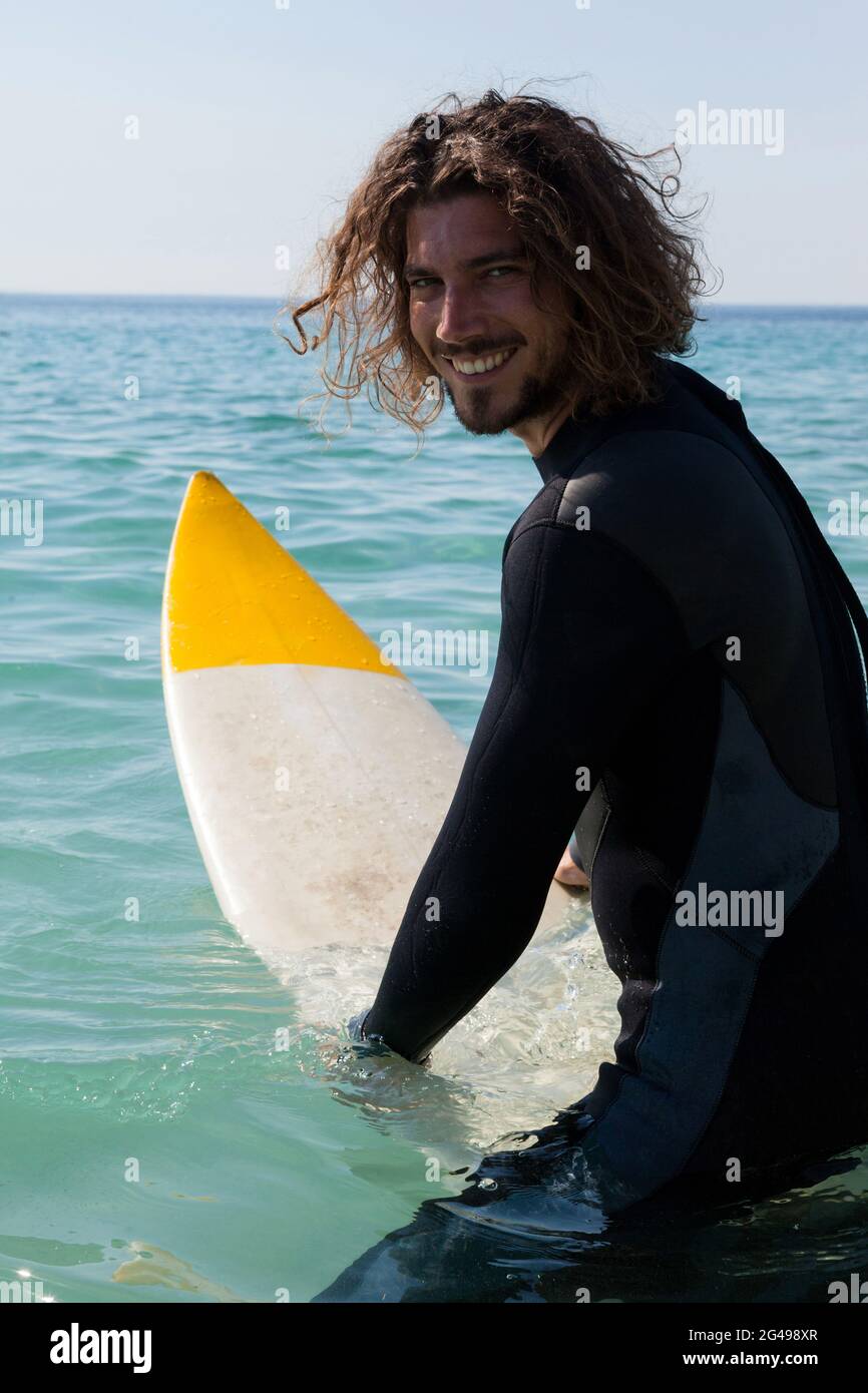 Smiling surfer sitting on surfboard at seacoast Stock Photo - Alamy