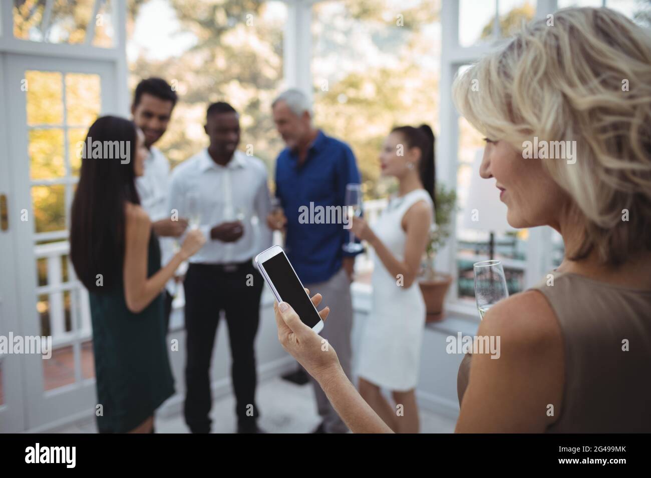 Woman using mobile phone while friends interacting in background Stock ... Woman using mobile phone while friends interacting in background Stock ...