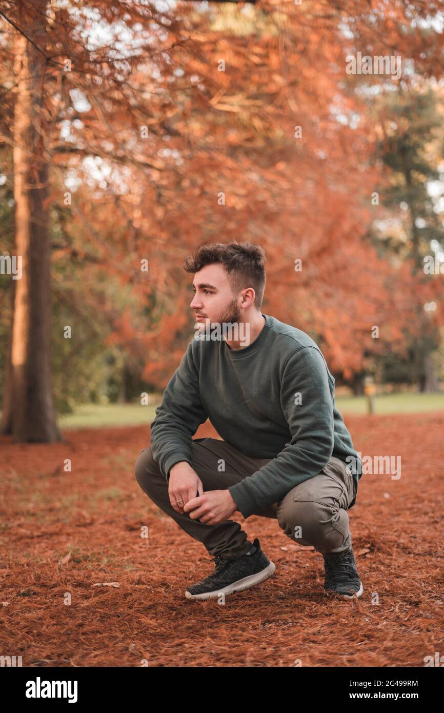A young attractive man crouched in a park Stock Photo - Alamy