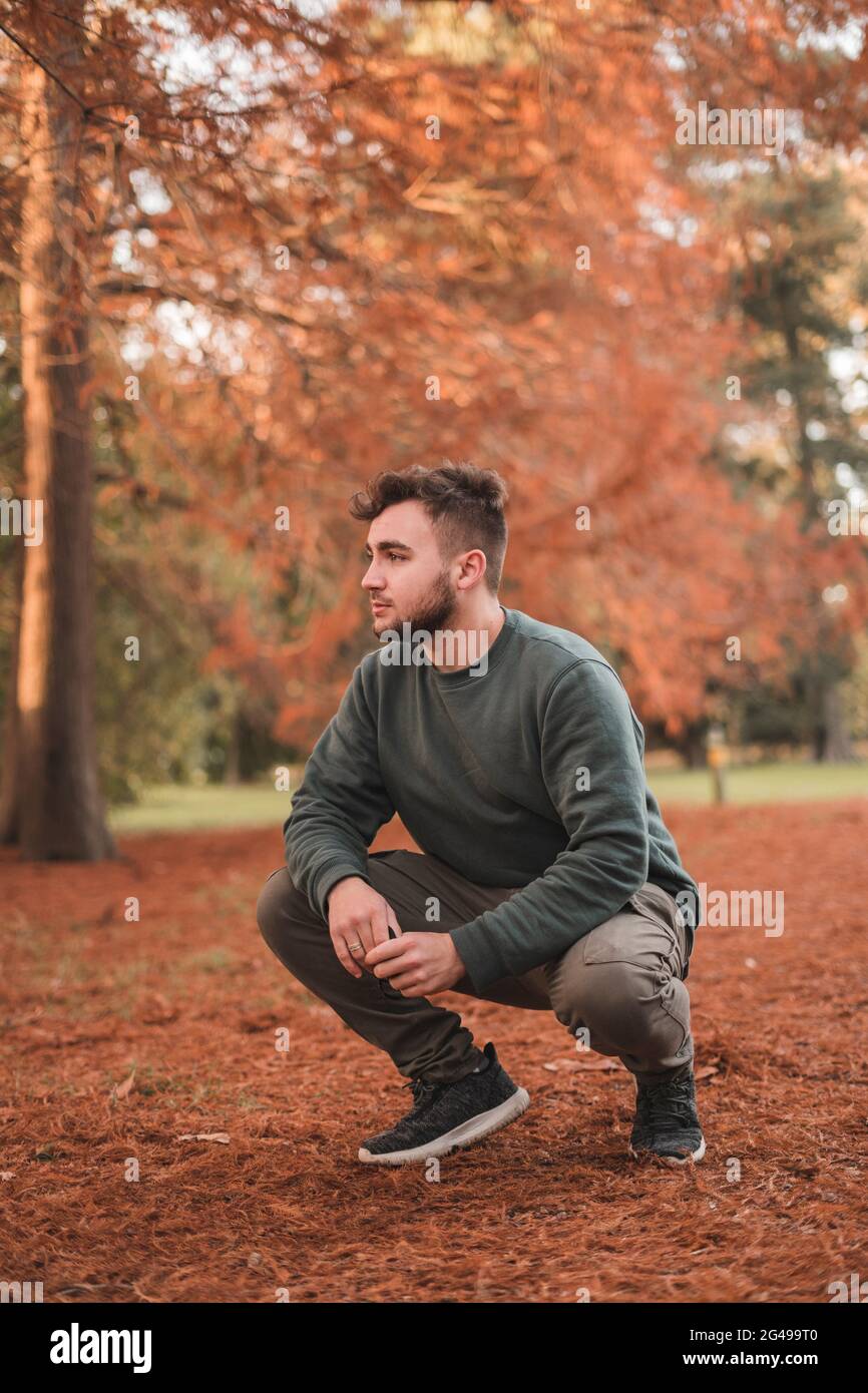 A young attractive man crouched in a park Stock Photo - Alamy