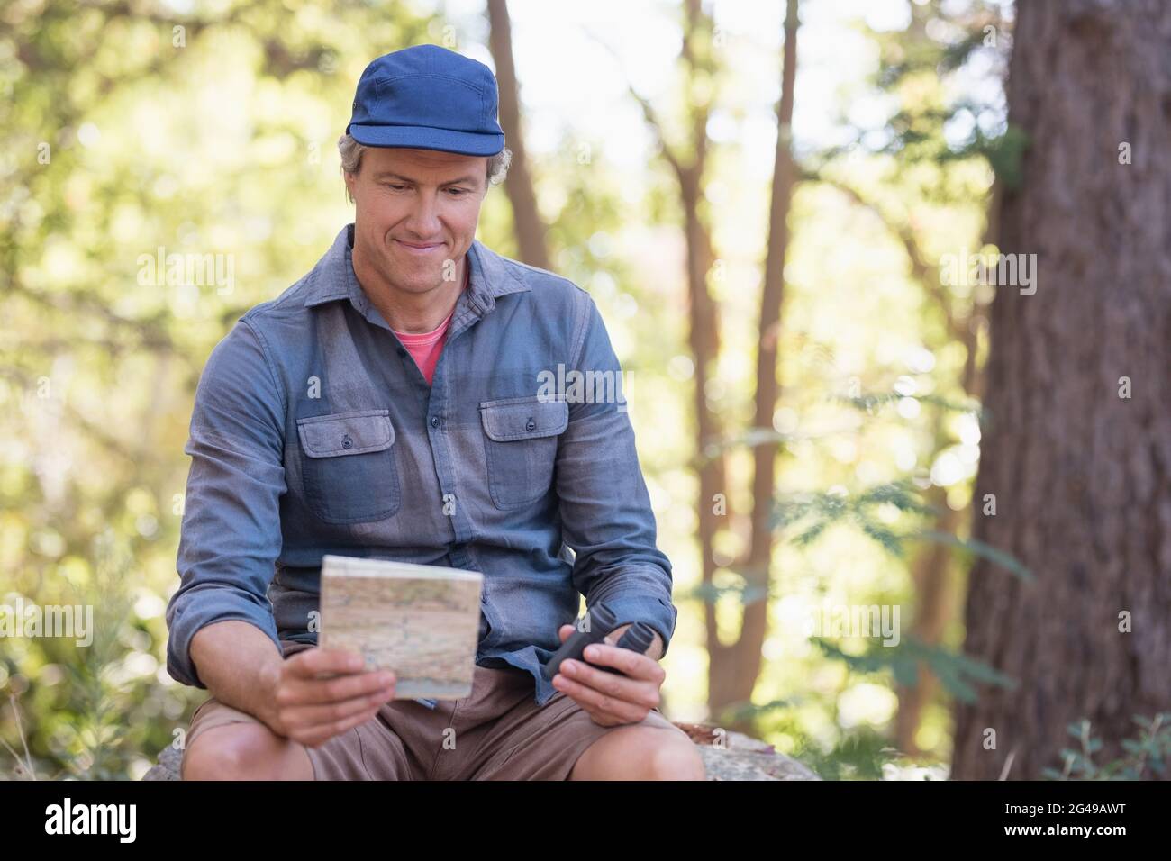 Happy hiker reading map while sitting on rock Stock Photo - Alamy