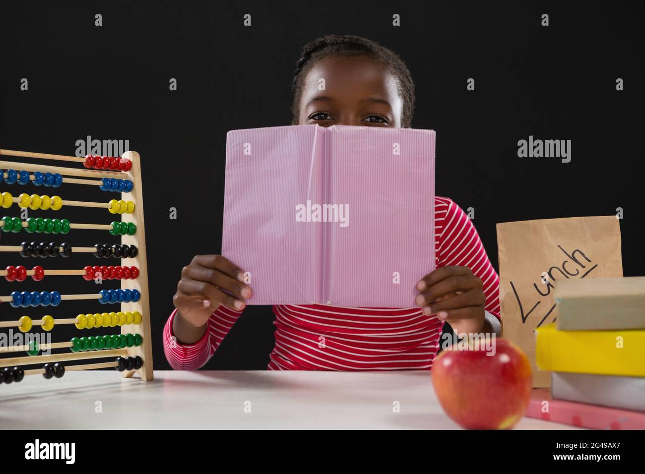 Schoolgirl hiding face behind book against black background Stock Photo ...