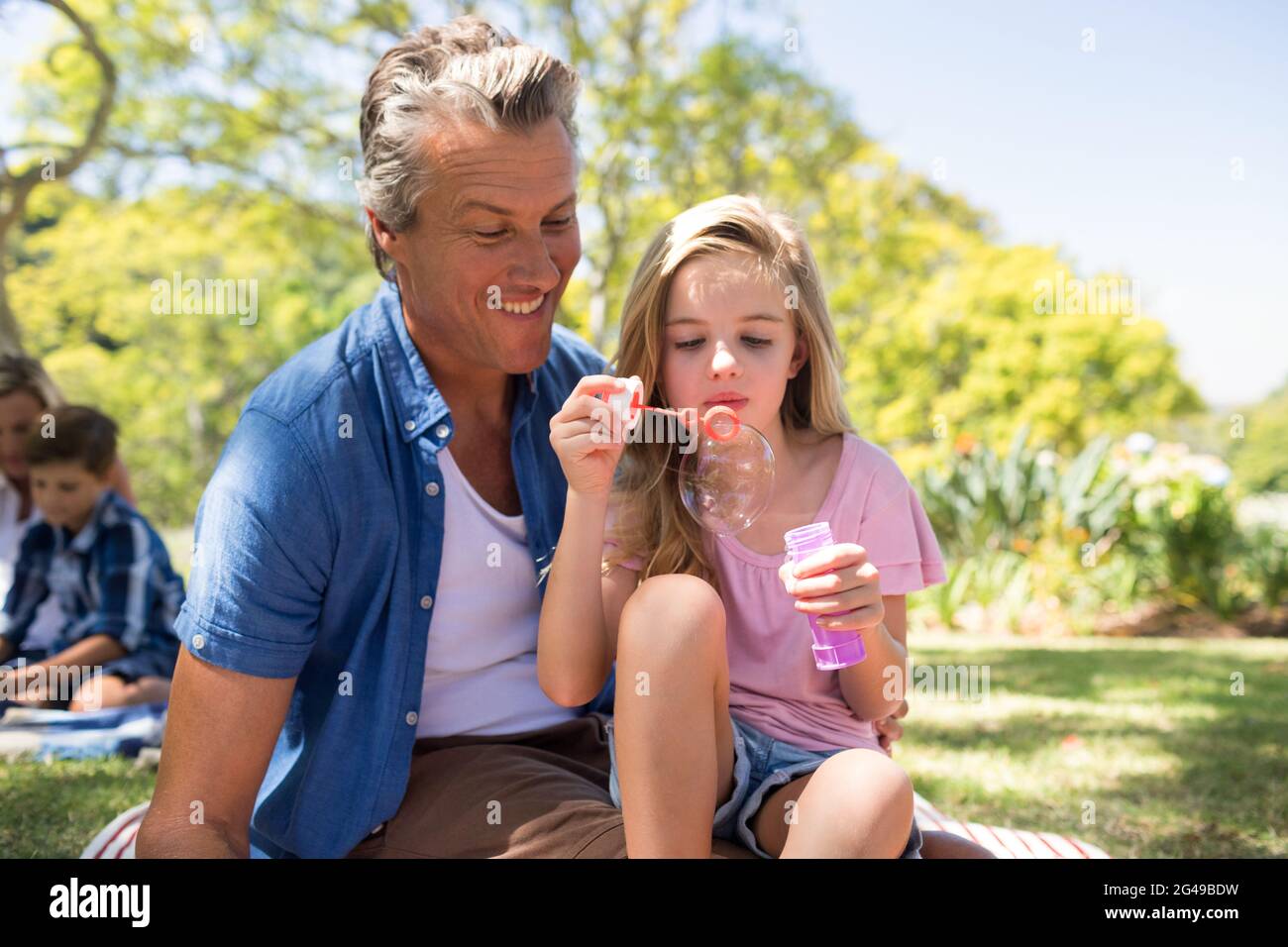 Father and daughter blowing bubble with bubble wand at picnic in park ...