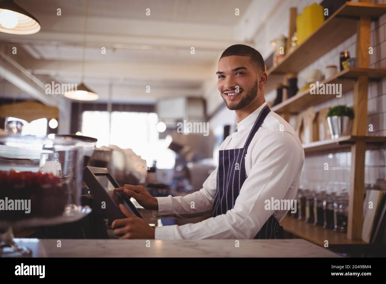 Smiling handsome young waiter using computer at counter Stock Photo - Alamy