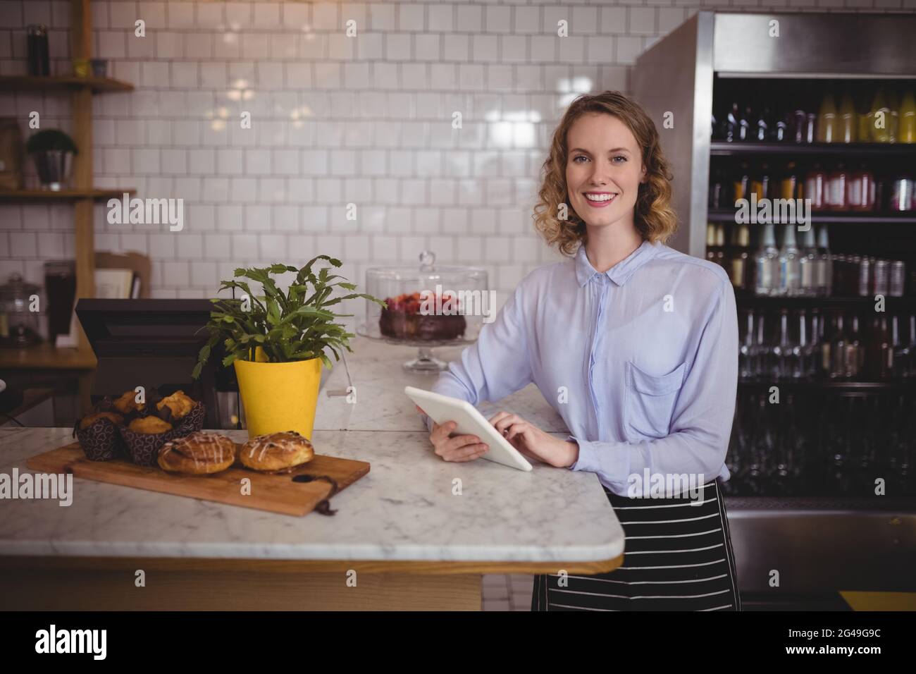 Portrait of attractive young waitress using digital tablet while ...