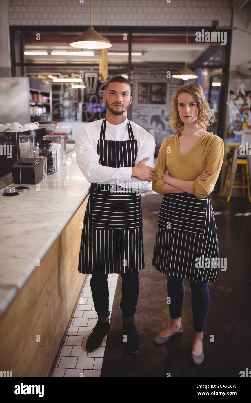 Portrait of confident young wait staff standing with arms crossed by ...