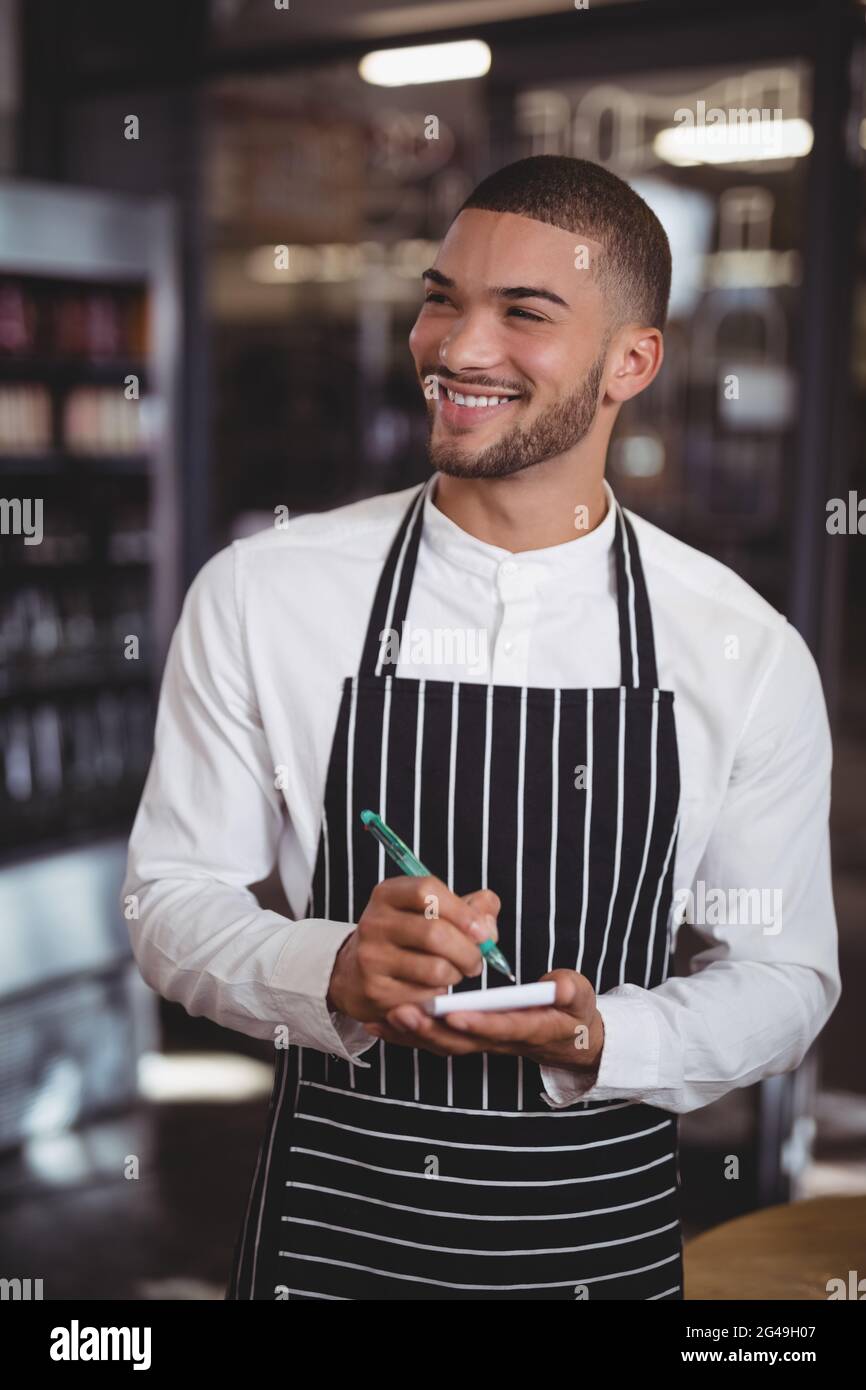 Smiling young waiter writing in notepad at coffee shop Stock Photo - Alamy