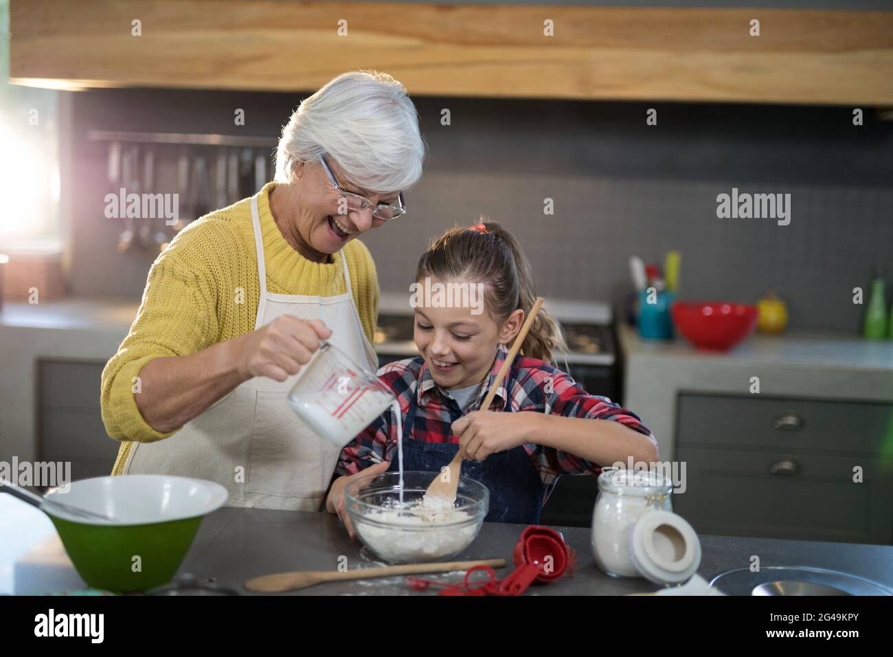 Grandmother adding water while granddaughter is mixing flour in a bowl ...