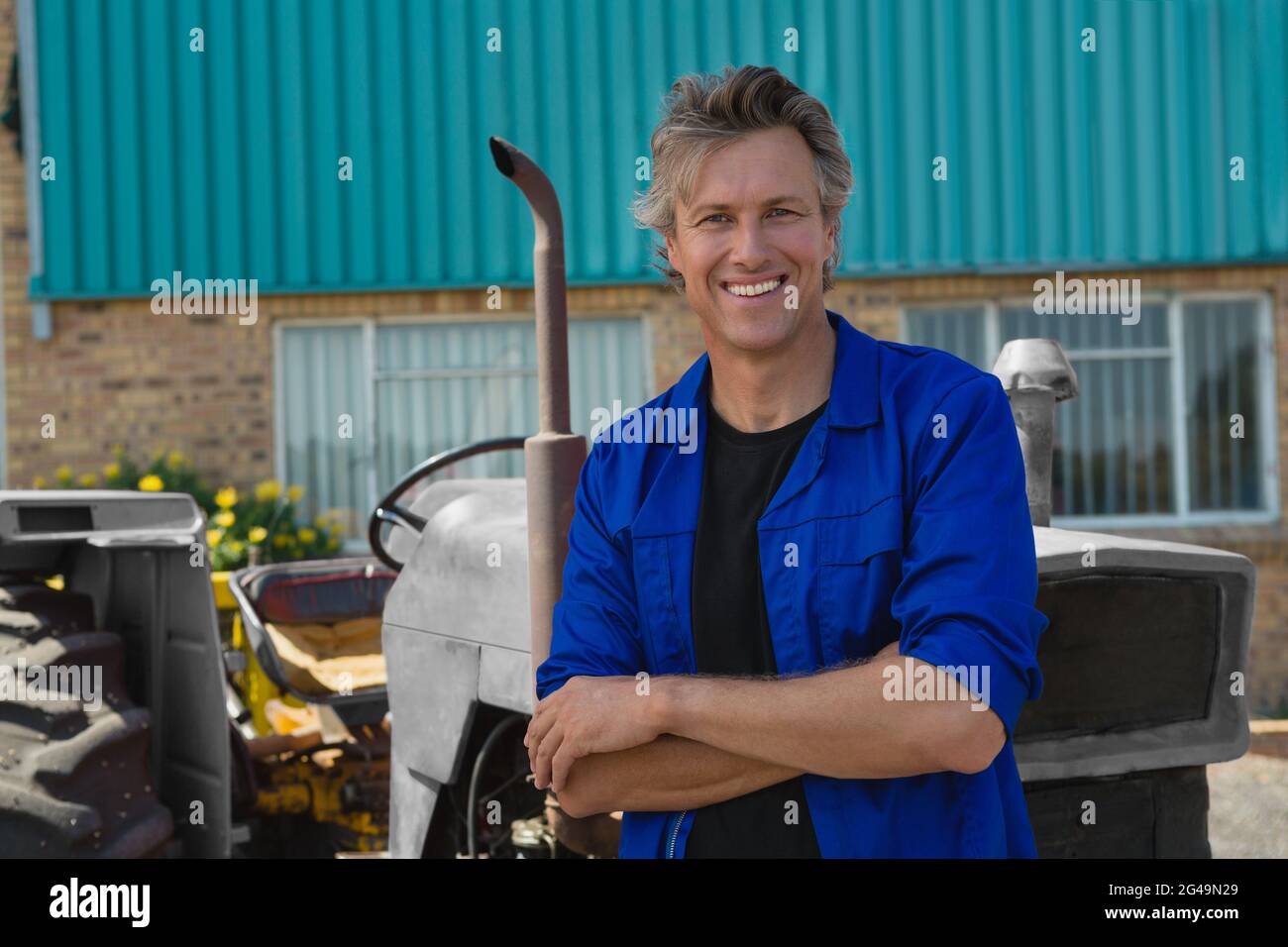 Worker standing with arms crossed near tractor Stock Photo - Alamy