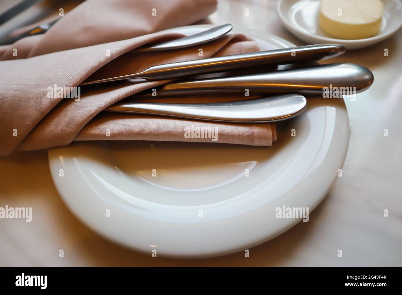 Table setting in the restaurant. White plate with cutlery in napkin on ...