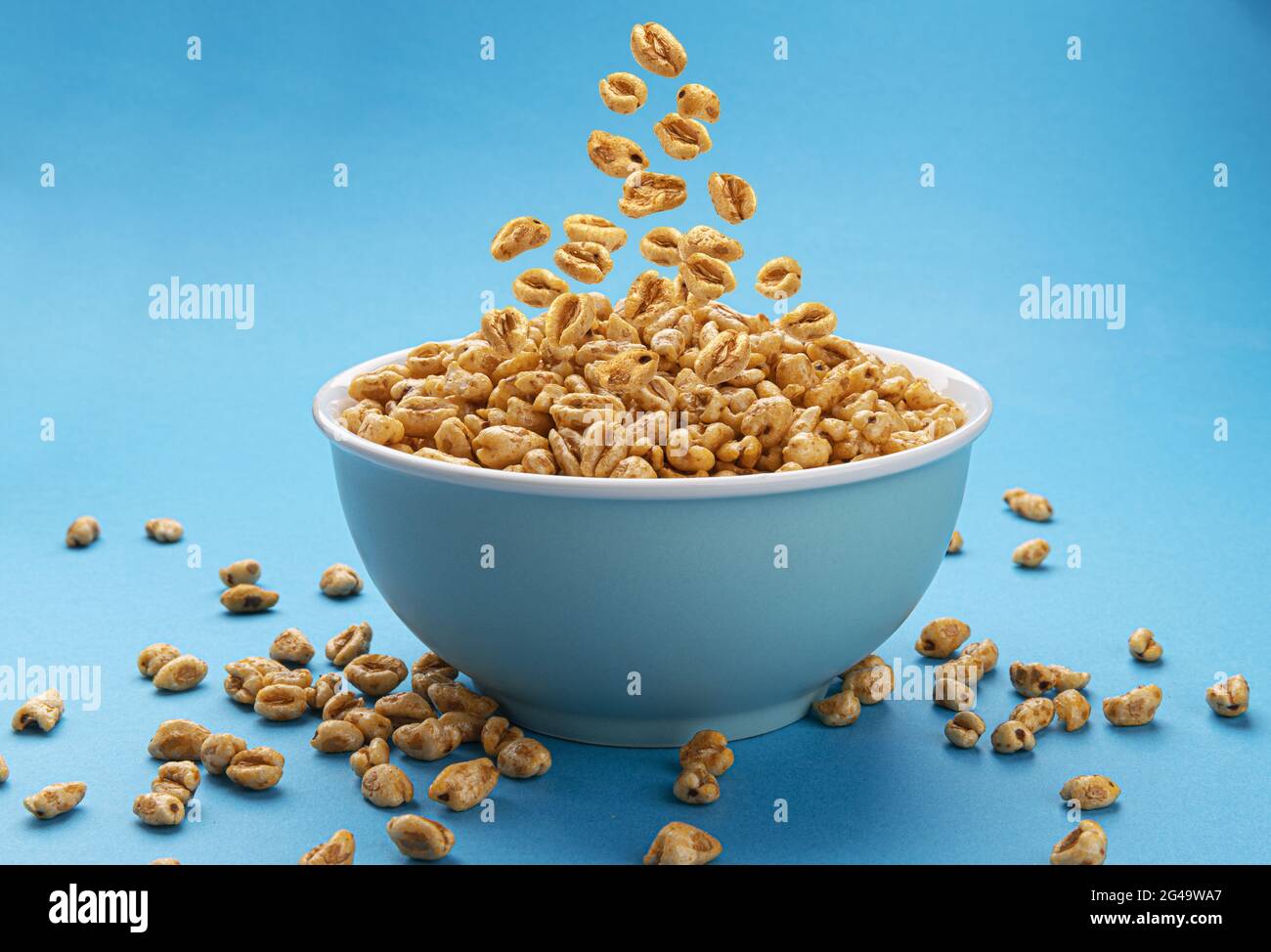 Falling puffed wheat cereal in bowl on blue background Stock Photo - Alamy